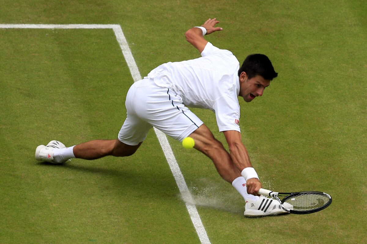 Photo : Novak Djokovic slides to make a shot against Roger Federer in ...